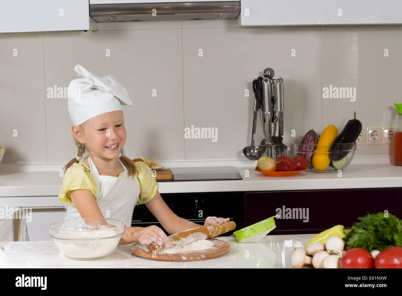 Happy little girl in a white chefs hat making pizza in the kitchen ...