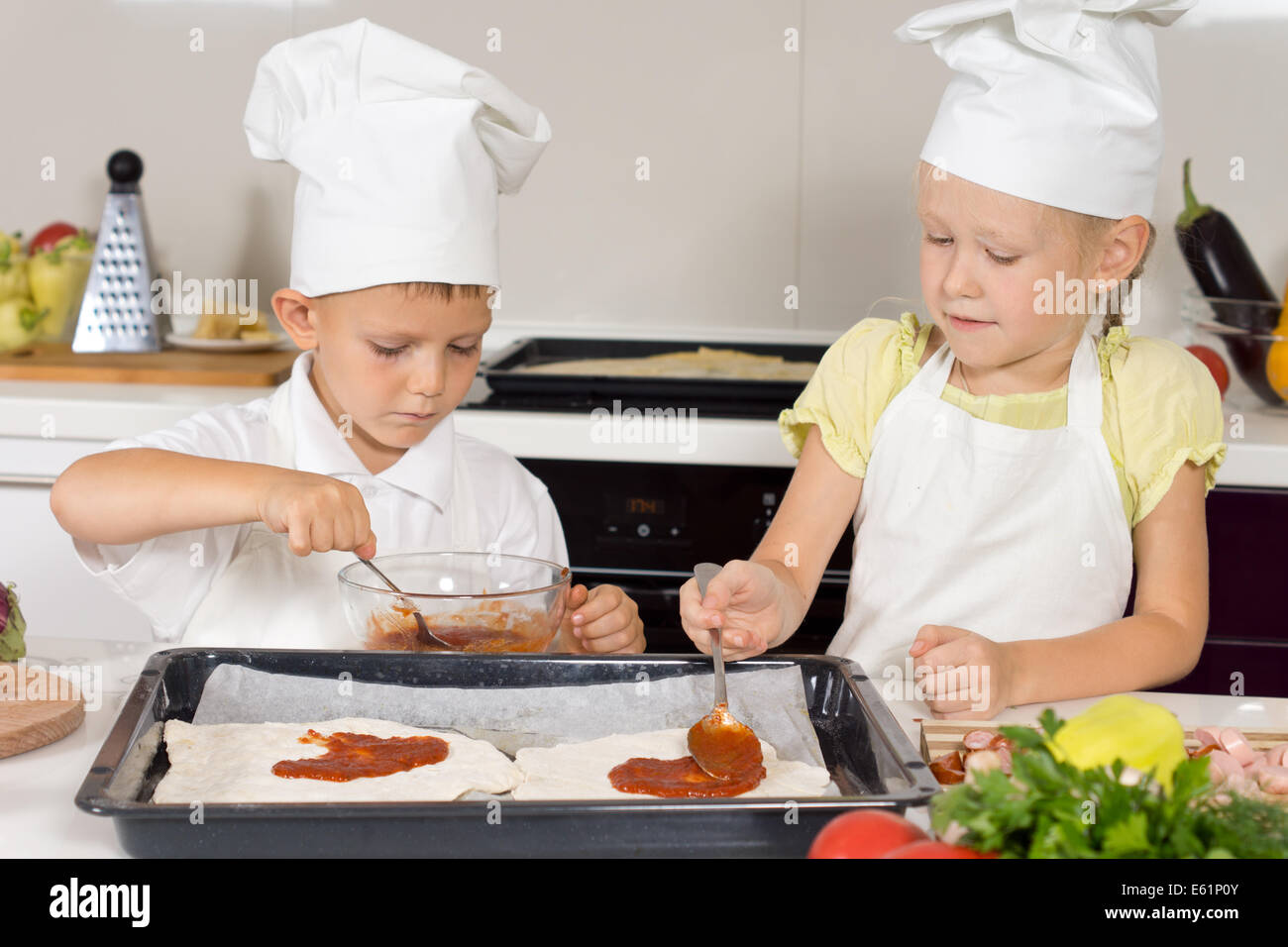 Two young children wearing chefs uniforms making themselves a homemade ...