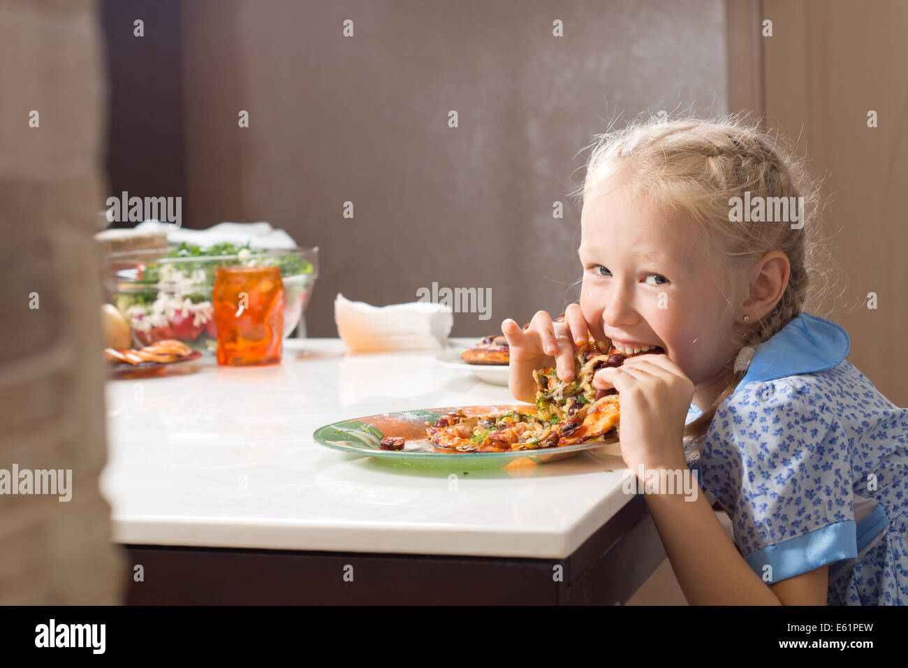 Hungry pretty little girl devouring homemade pizza looking up from ...