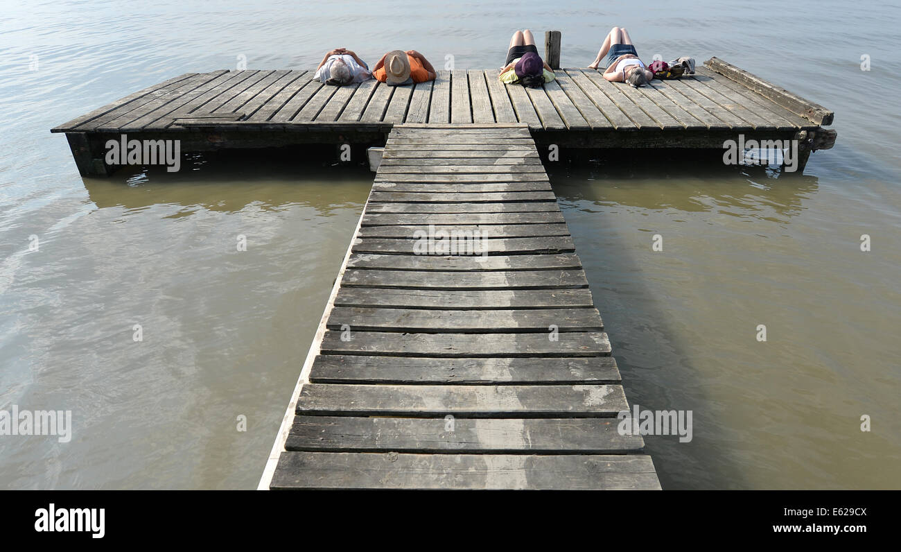 A group of sunbathers enjoy the warm sun on a jetty stretching out on ...