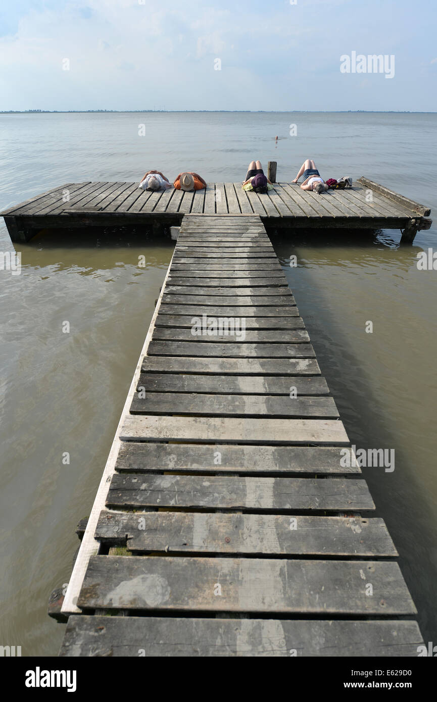 A group of sunbathers enjoy the warm sun on a jetty stretching out on ...