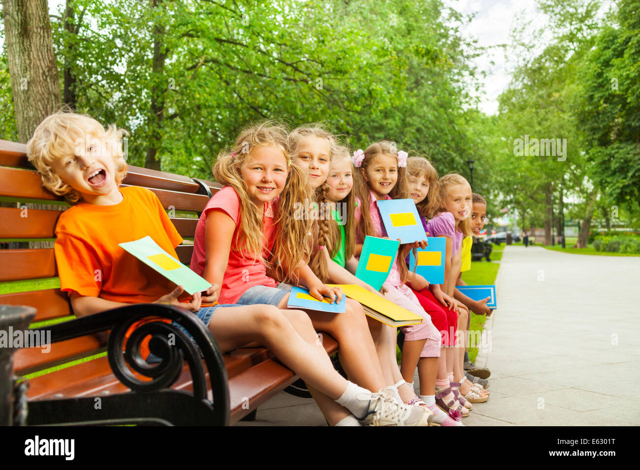 Kids with blue notebooks sit in row on bench Stock Photo - Alamy