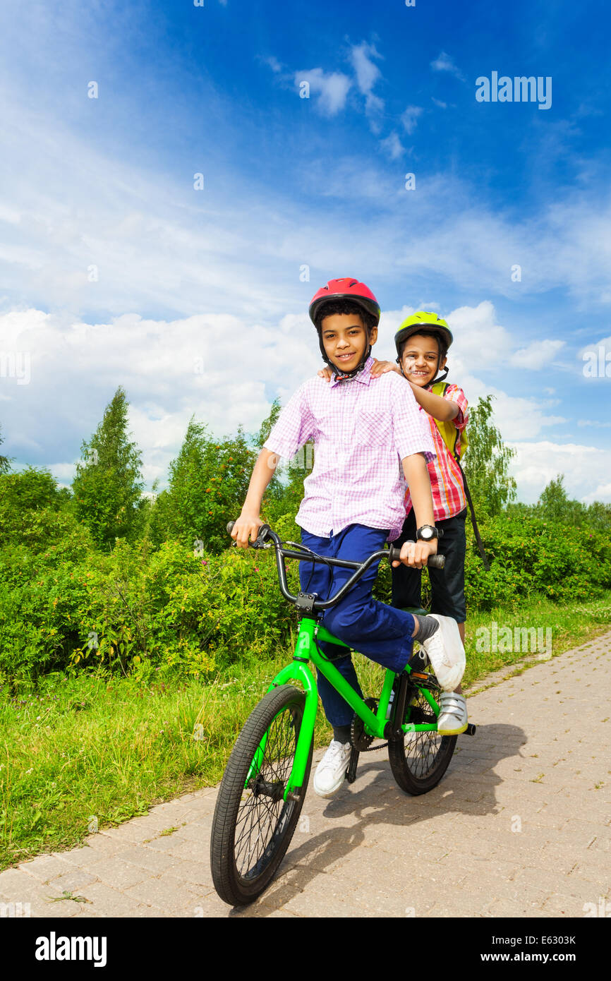 Two happy boys riding same bike both standing Stock Photo - Alamy