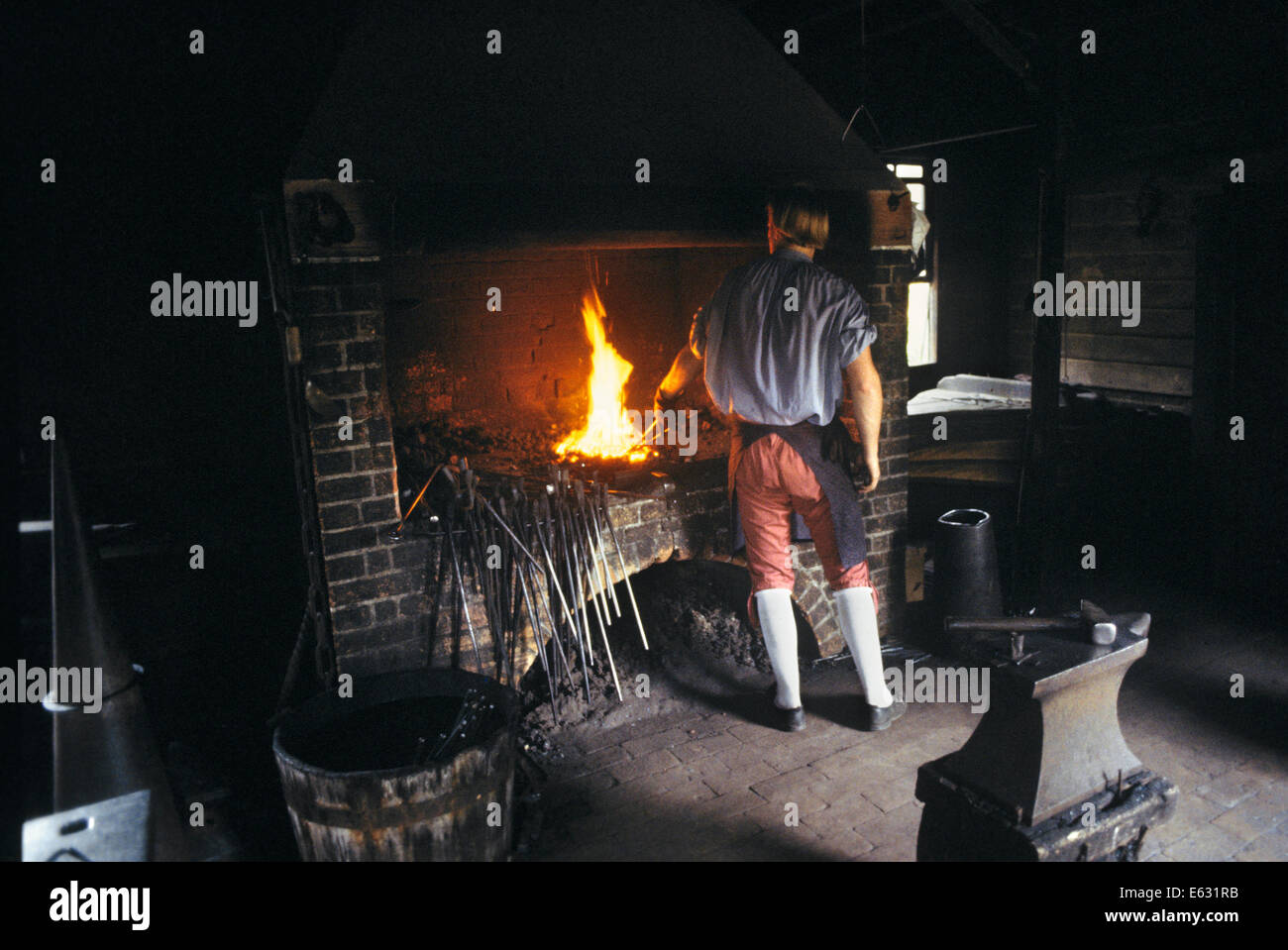 ANONYMOUS BLACKSMITH WEARING COLONIAL CLOTHES BACK TO CAMERA HOLDING ...