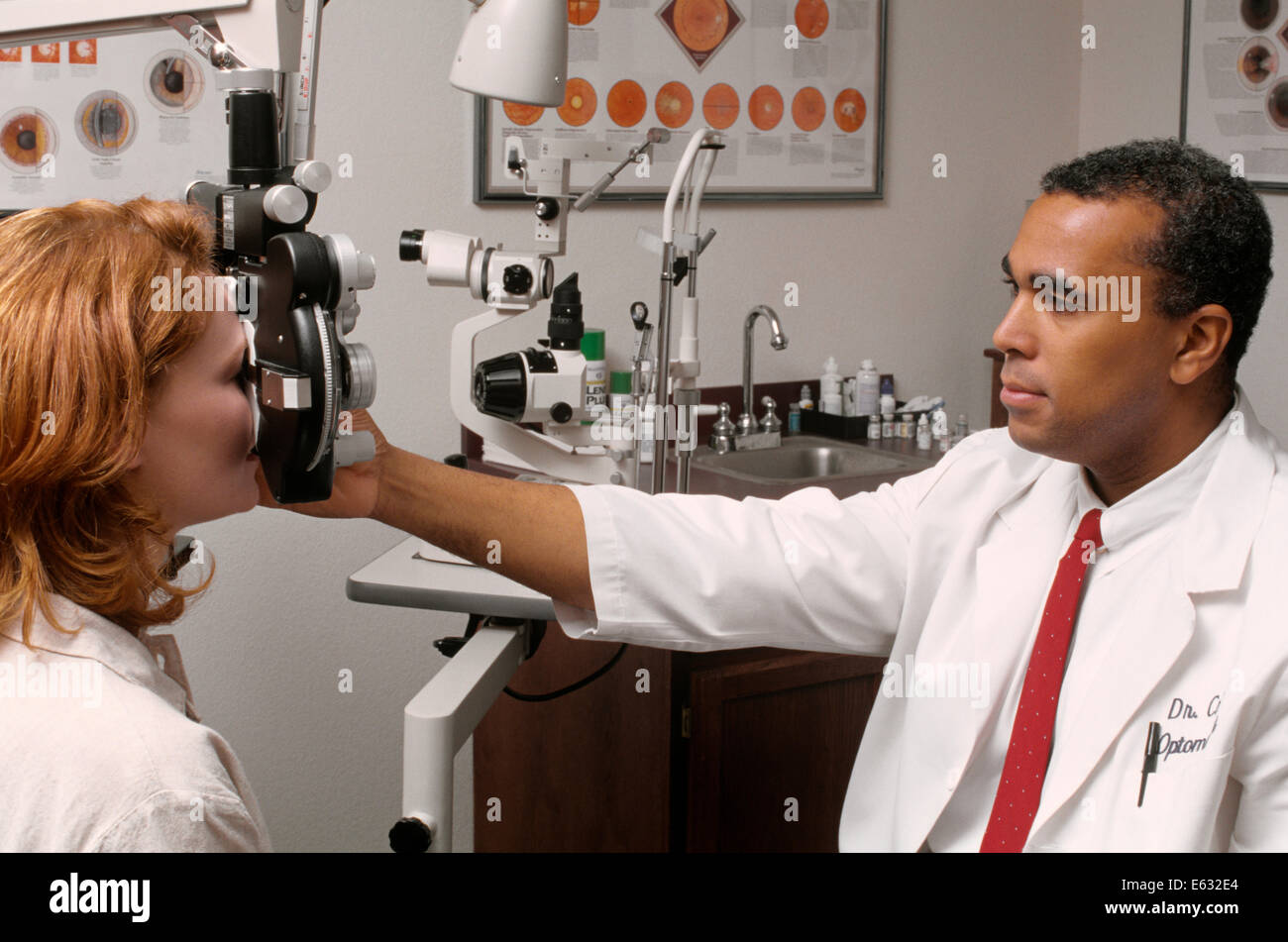 1990s AFRICAN AMERICAN OPTOMETRIST EXAMINING RED HAIRED WOMAN'S EYES ...