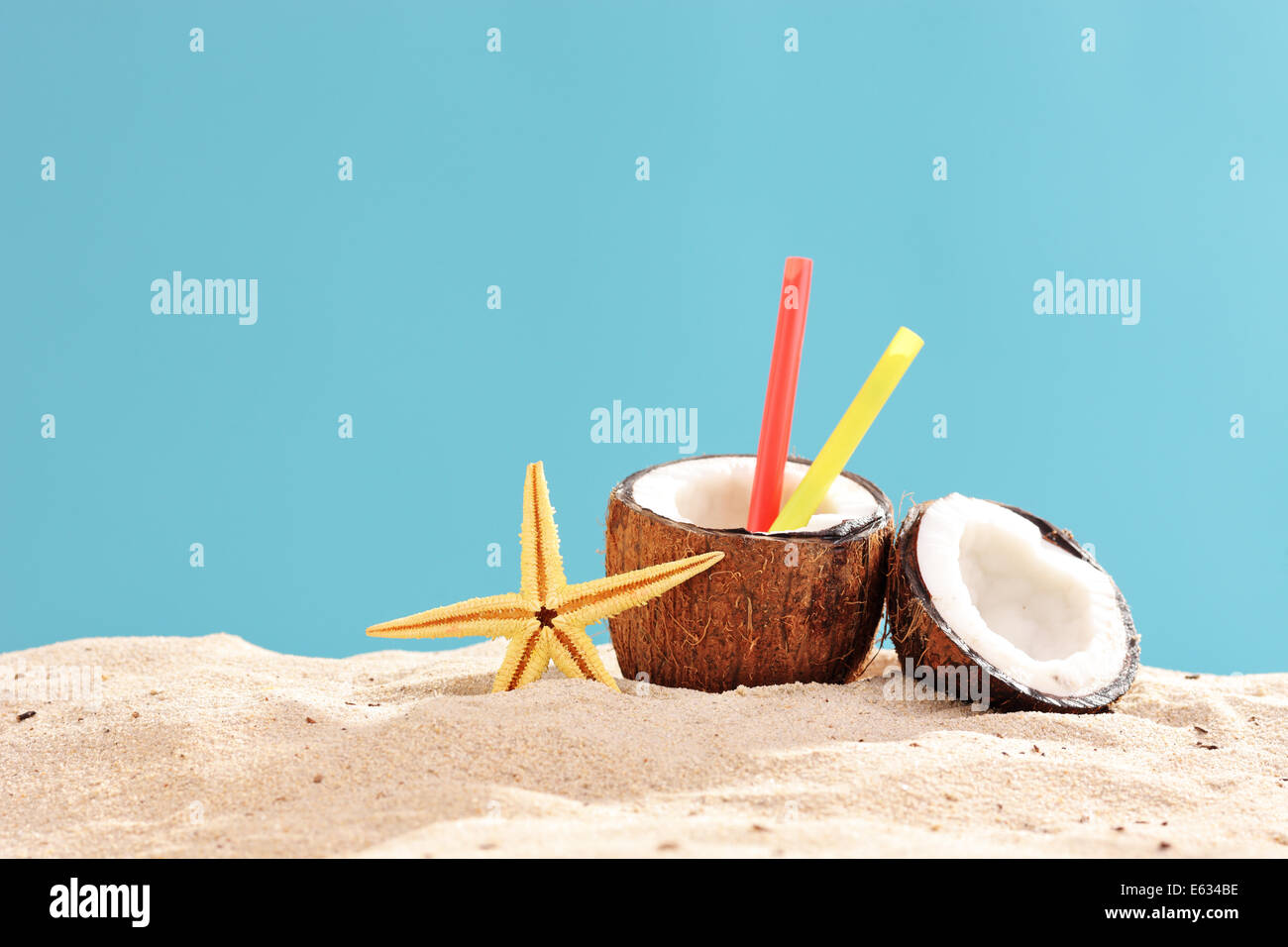 Exotic cocktail in a coconut shell on a sandy surface on blue ...