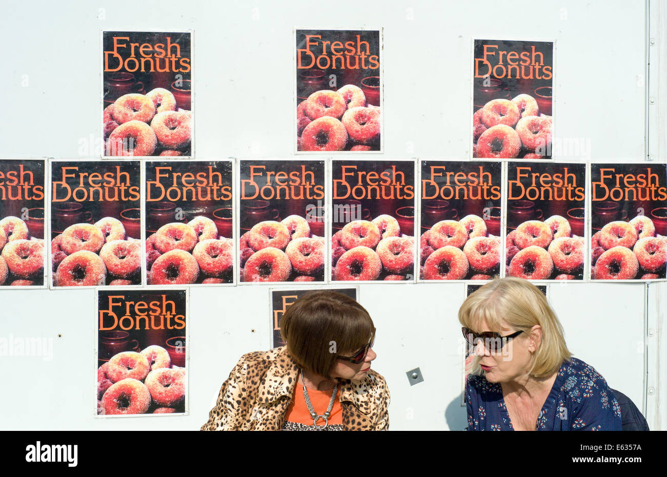 Two Women talking under adverts for doughnuts Stock Photo - Alamy