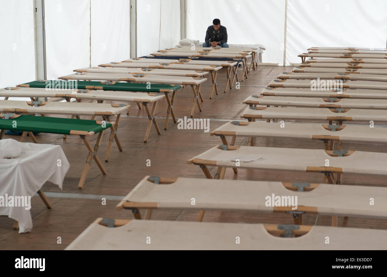 An refugee from Africa sits on his bed in a tent of a refugee first ...