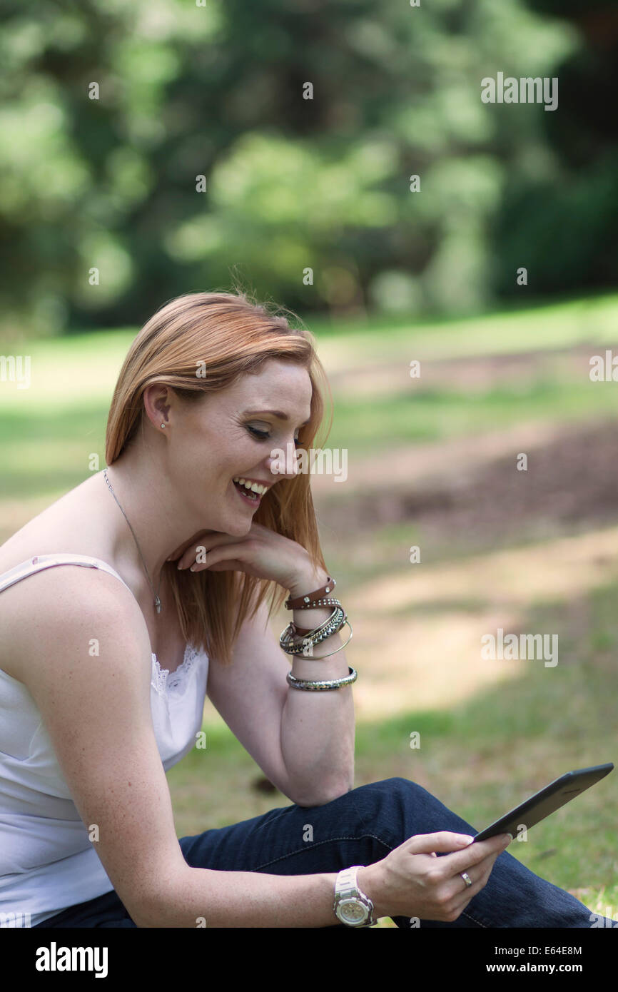 A young woman reading a funny ereader book in the park Stock Photo - Alamy