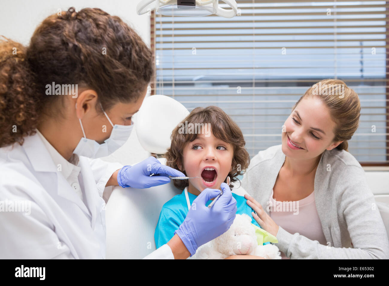 Pediatric dentist examining a little boys teeth with his mother Stock ...