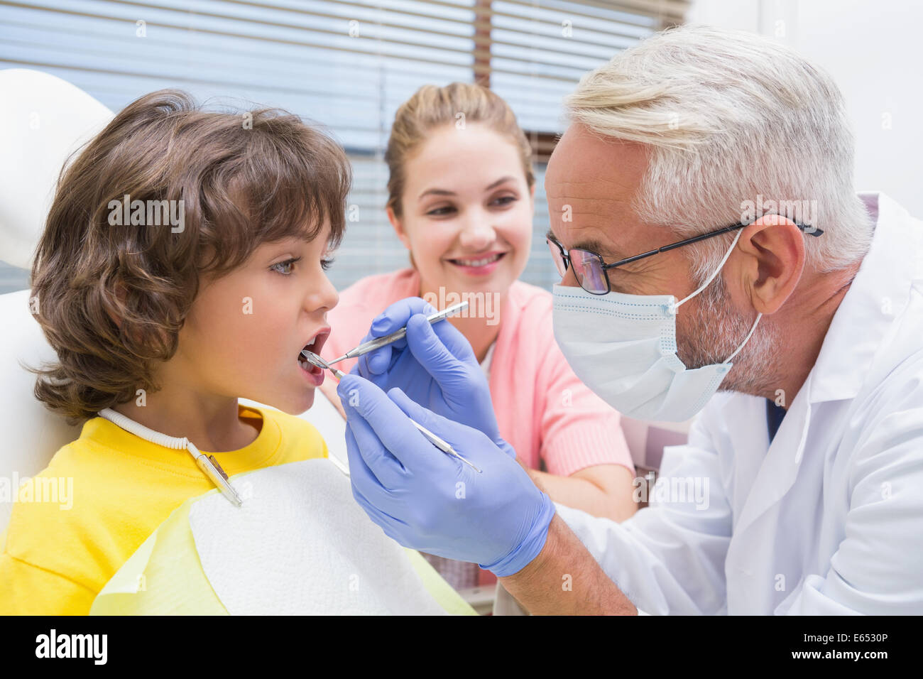 Pediatric dentist examining a little boys teeth with his mother ...