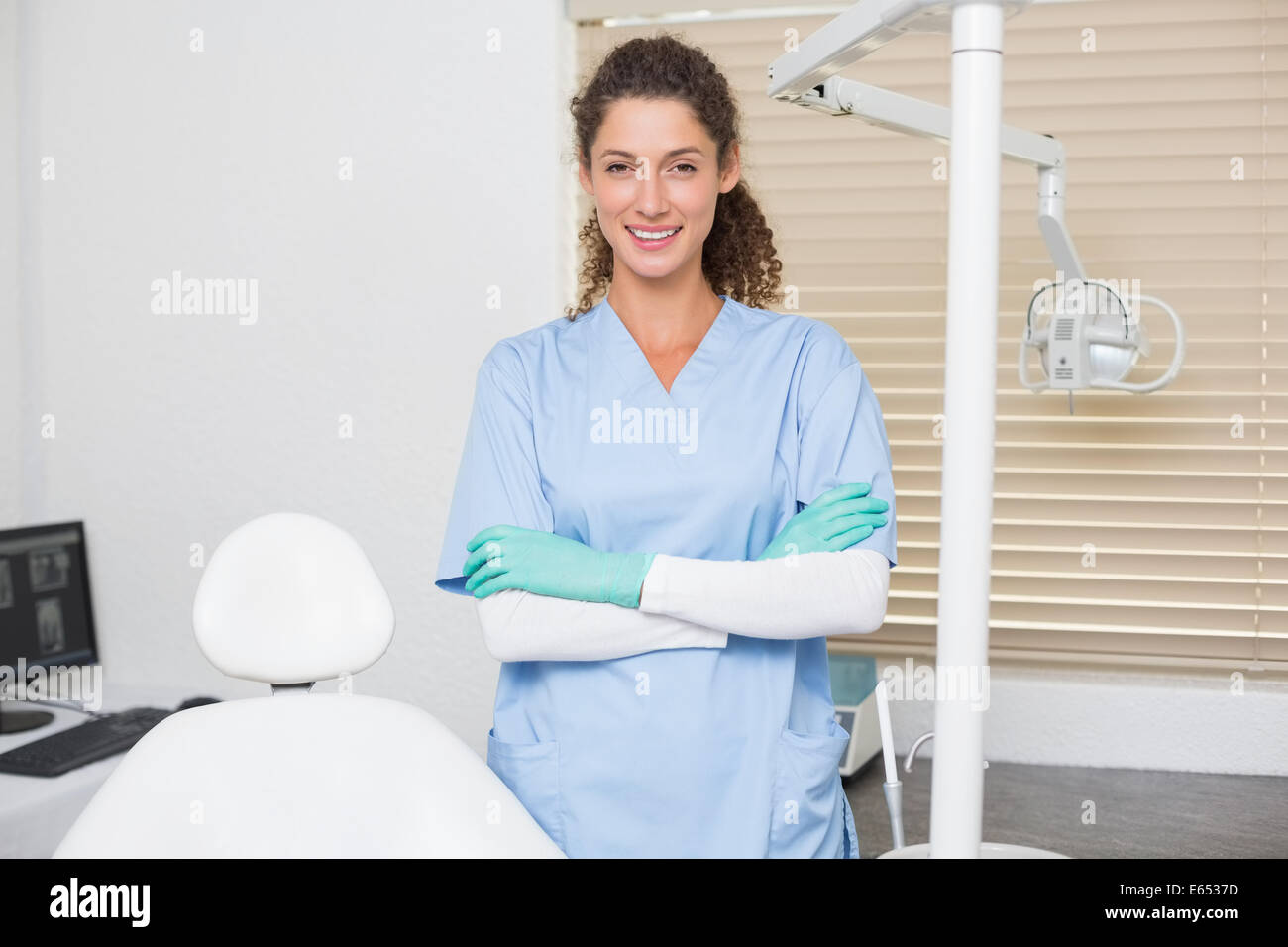 Dentist in blue scrubs smiling at camera beside chair Stock Photo - Alamy