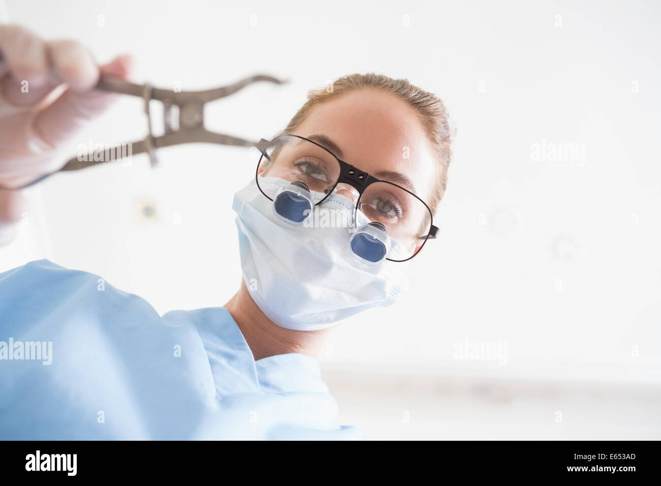 Dentist in surgical mask and dental loupes holding pliers over patient ...