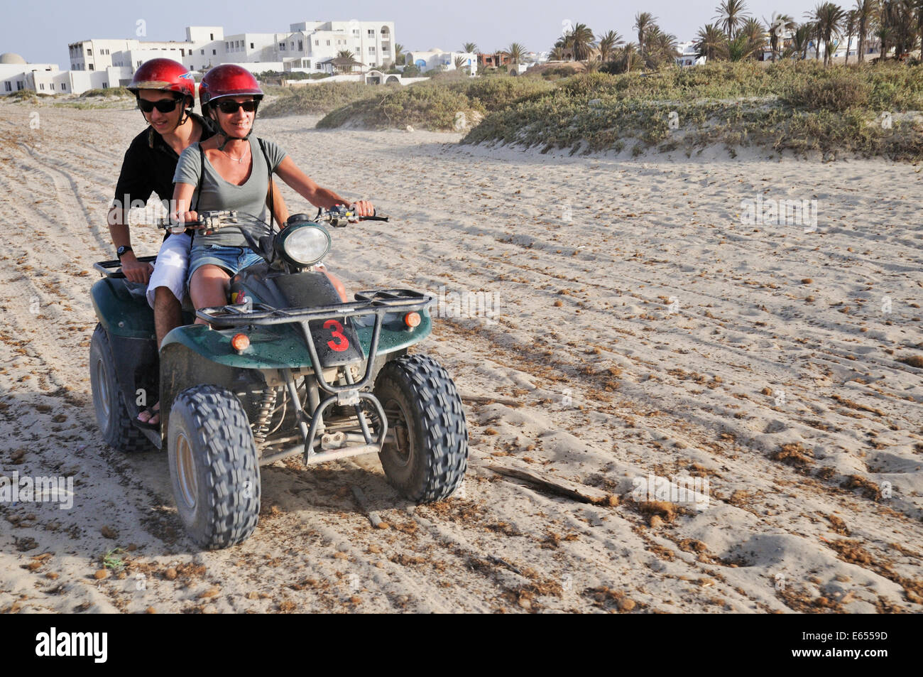 Woman and her teenager son riding on an ATV quad bike on the beach ...