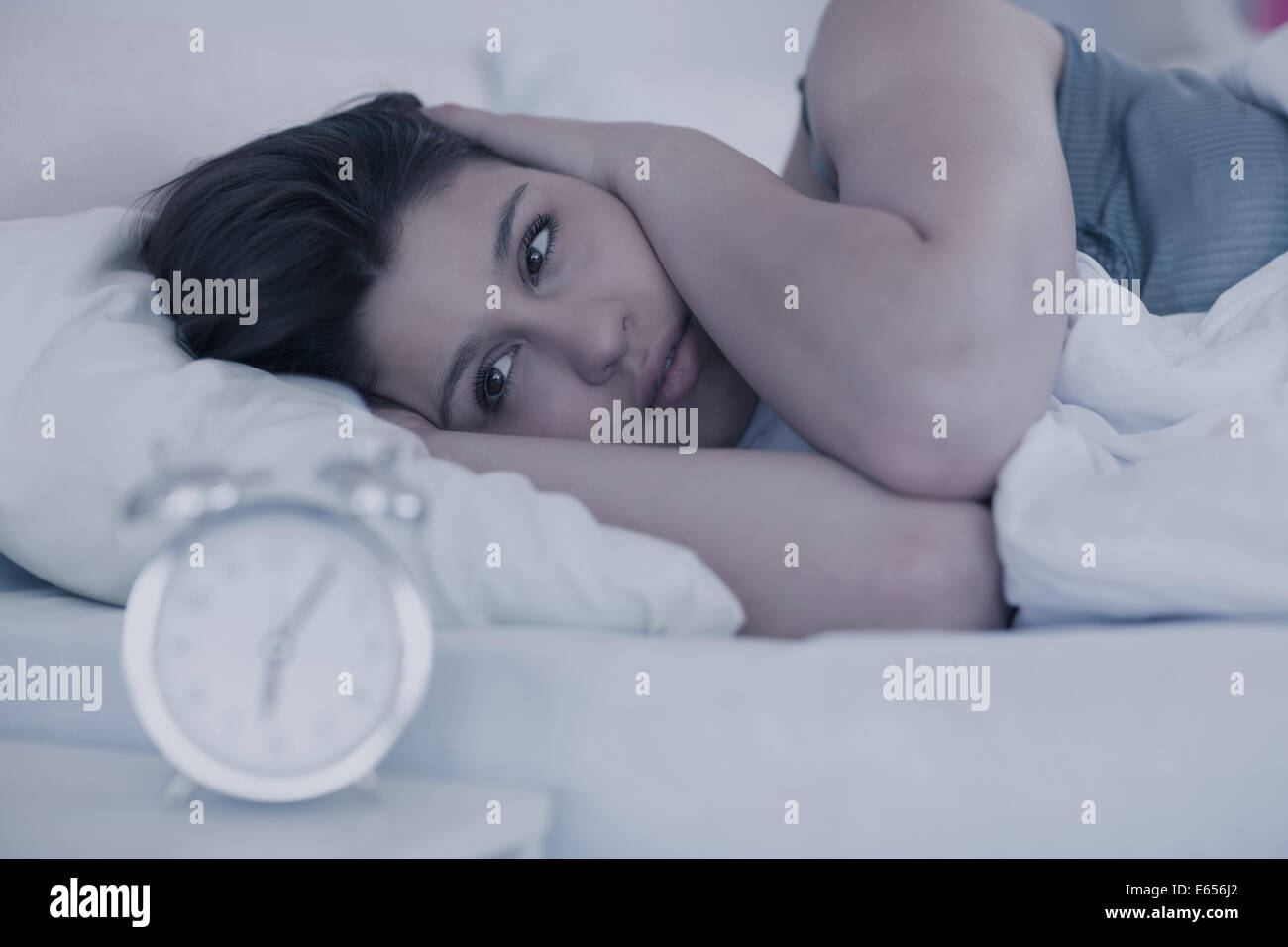 Beautiful brunette looking at alarm clock in her bed Stock Photo - Alamy