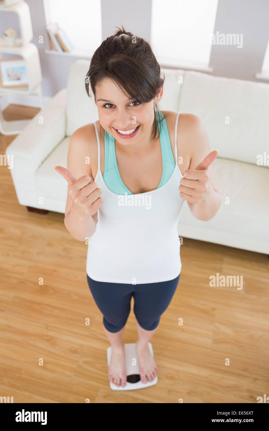 Fit brunette smiling at camera on the weighing scales Stock Photo - Alamy
