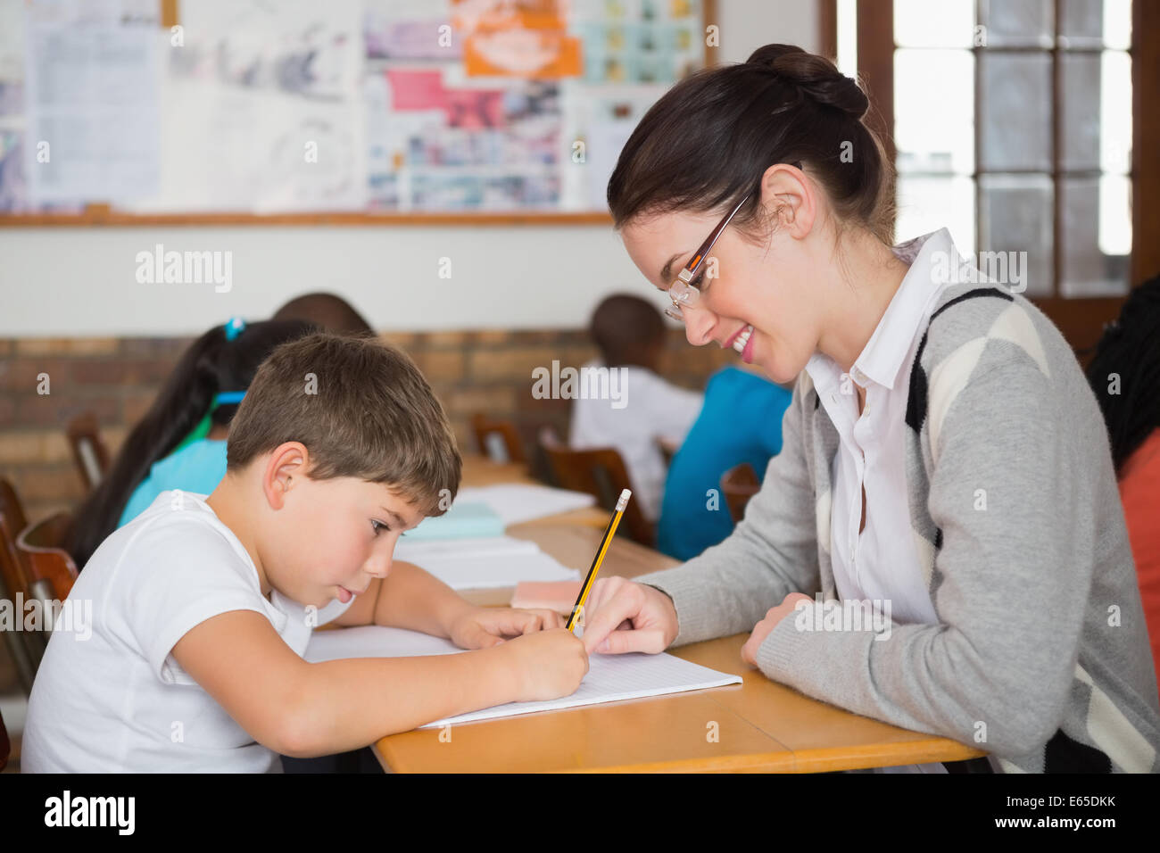 Pretty teacher helping pupil in classroom Stock Photo - Alamy