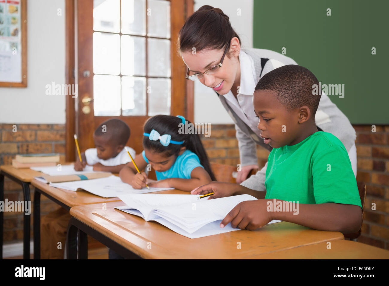 Pretty teacher helping pupil in classroom Stock Photo - Alamy