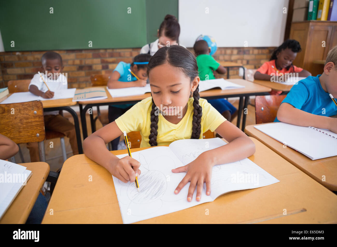 Cute pupils writing at desk in classroom Stock Photo - Alamy