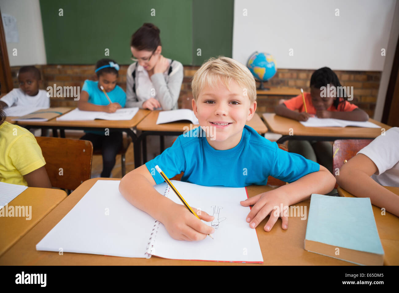 Cute pupils writing at desk in classroom Stock Photo - Alamy