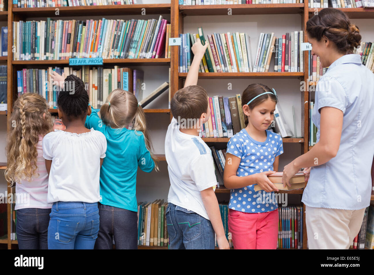 Cute pupils and teacher looking for books in library Stock Photo - Alamy