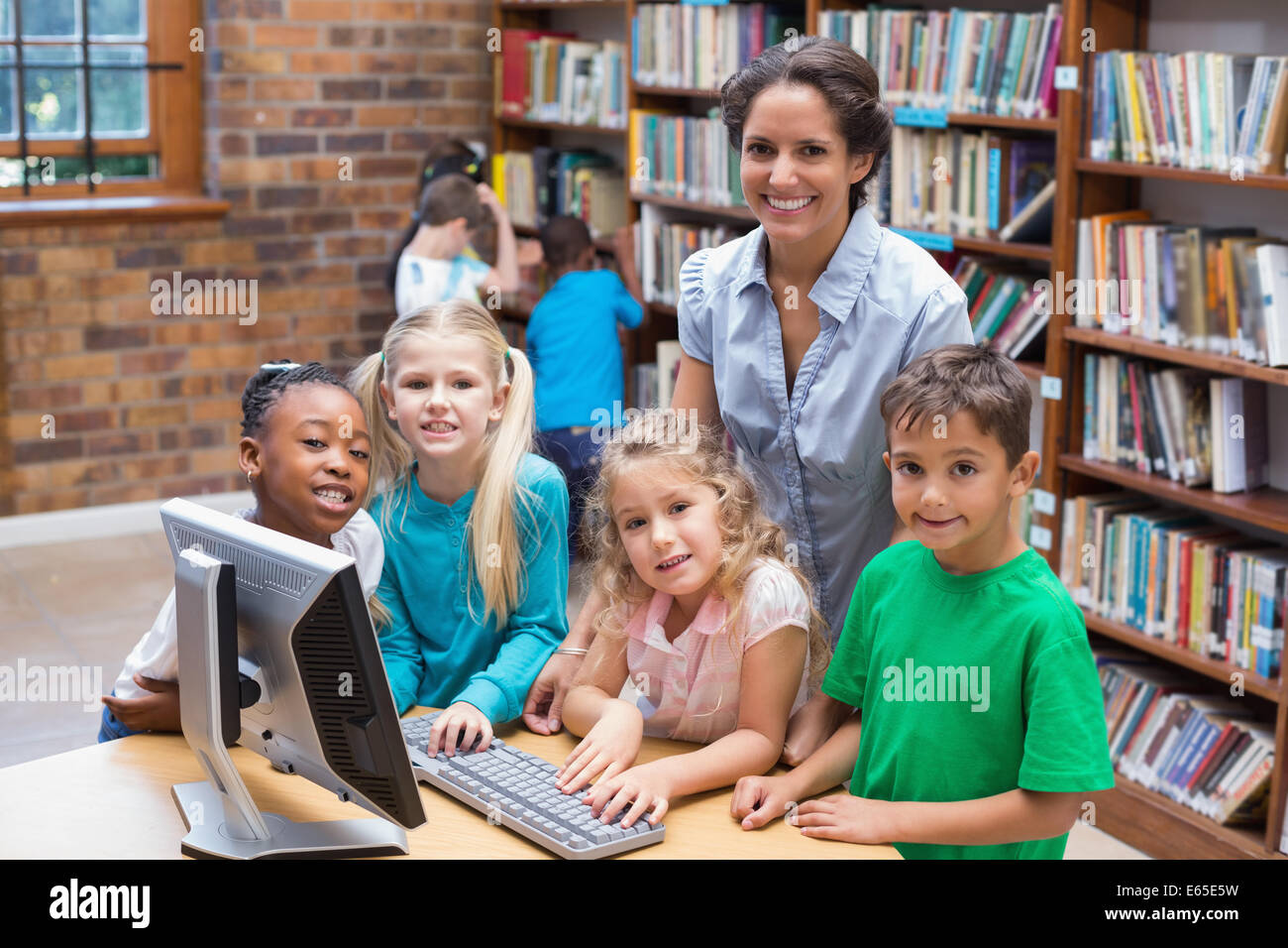 Cute pupils and teacher looking at computer in library Stock Photo - Alamy