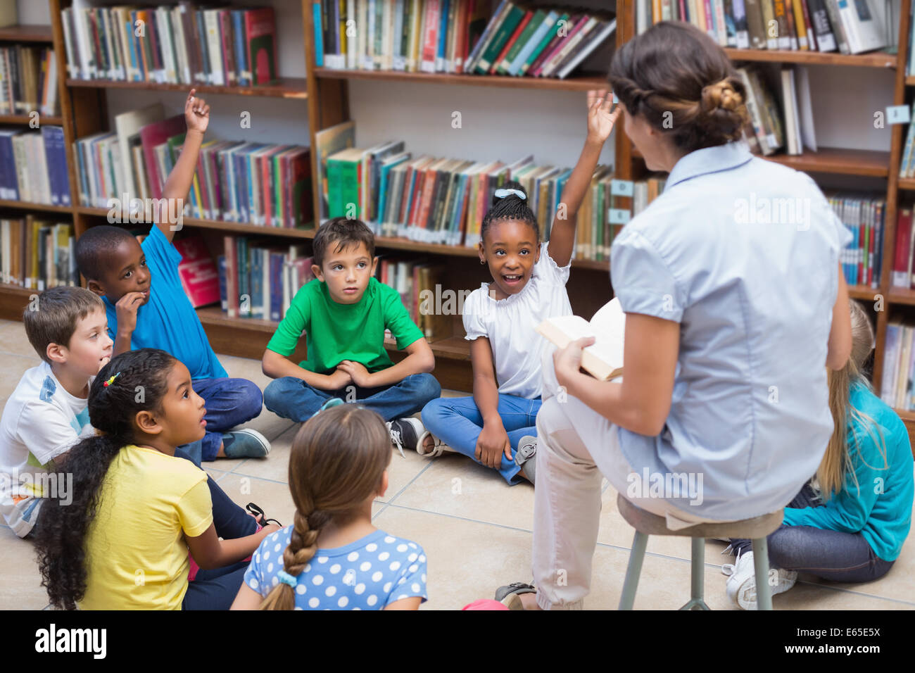 Cute pupils and teacher having class in library Stock Photo - Alamy