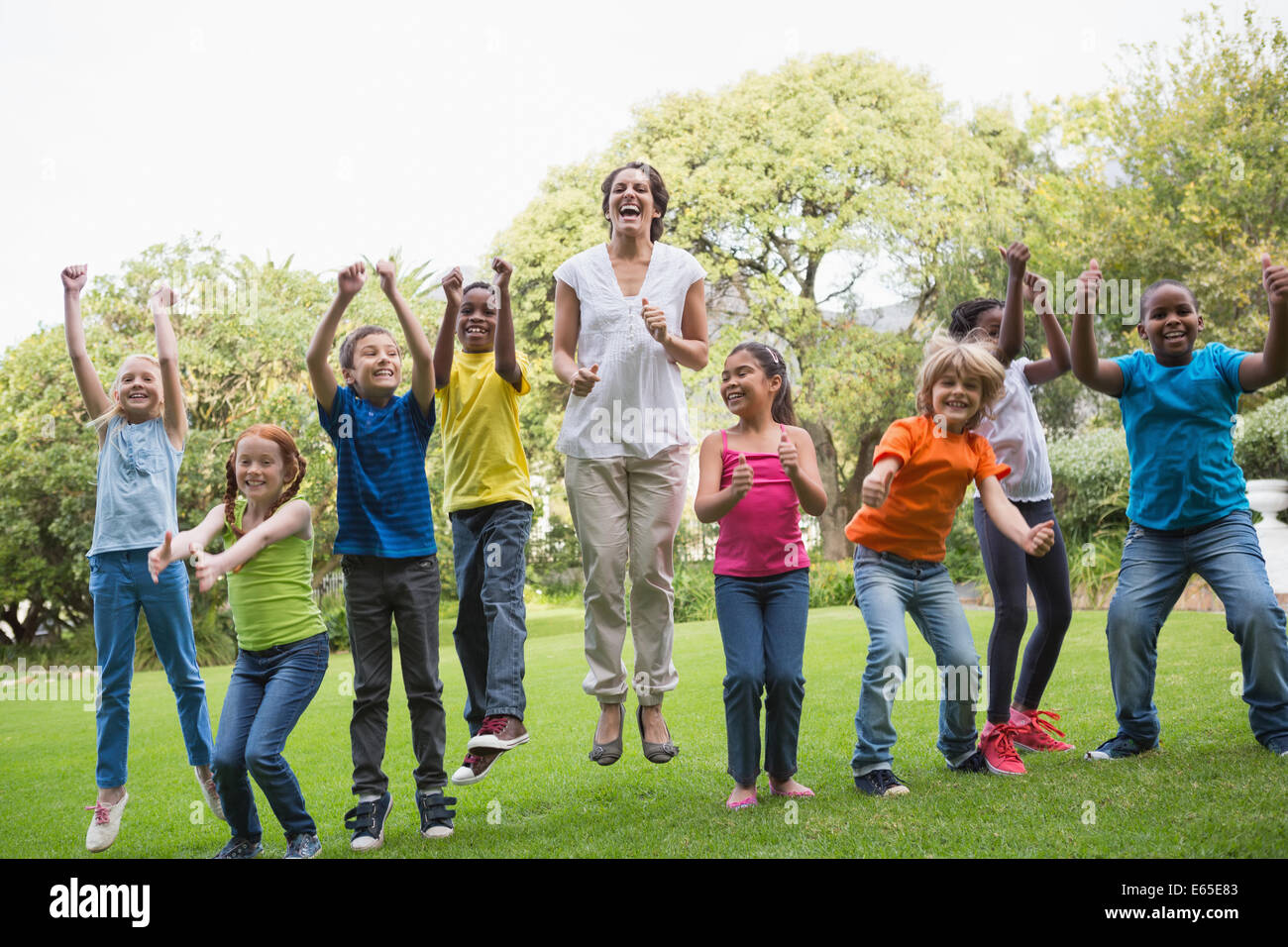 Pretty teacher jumping with pupils outside Stock Photo - Alamy