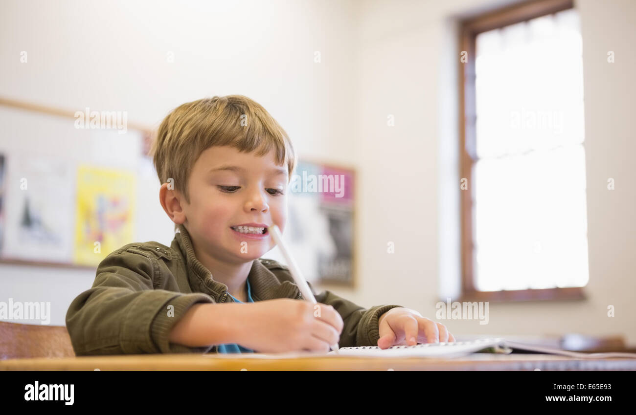 Happy pupil writing in notepad at his desk Stock Photo - Alamy