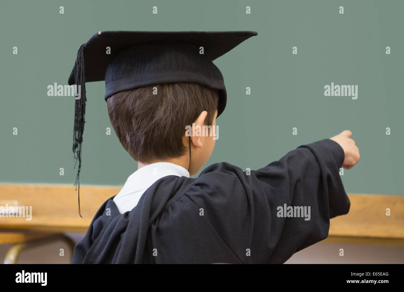 Cute pupil in graduation robe pointing in classroom Stock Photo - Alamy