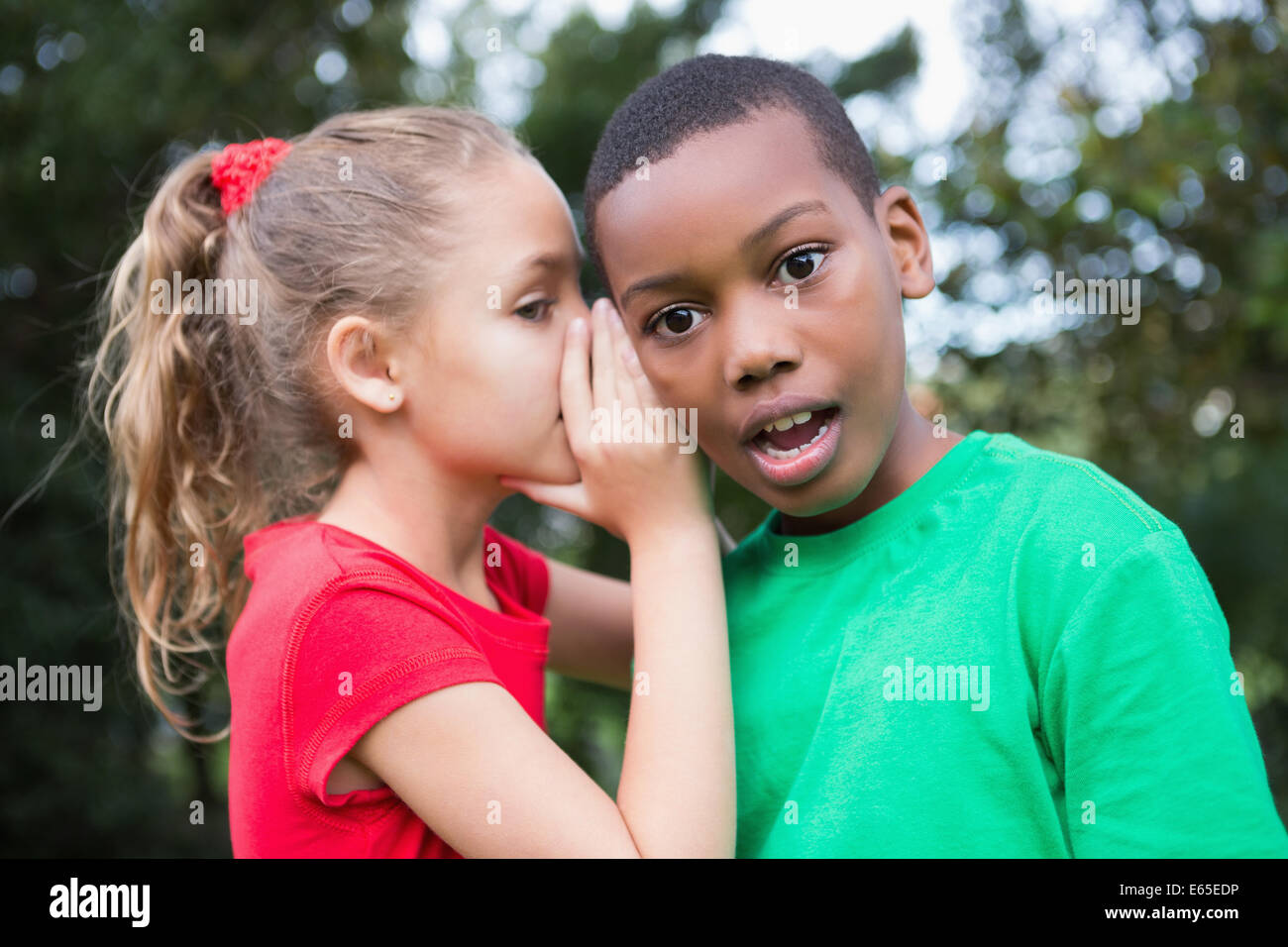 Cute children sharing gossip outside Stock Photo - Alamy
