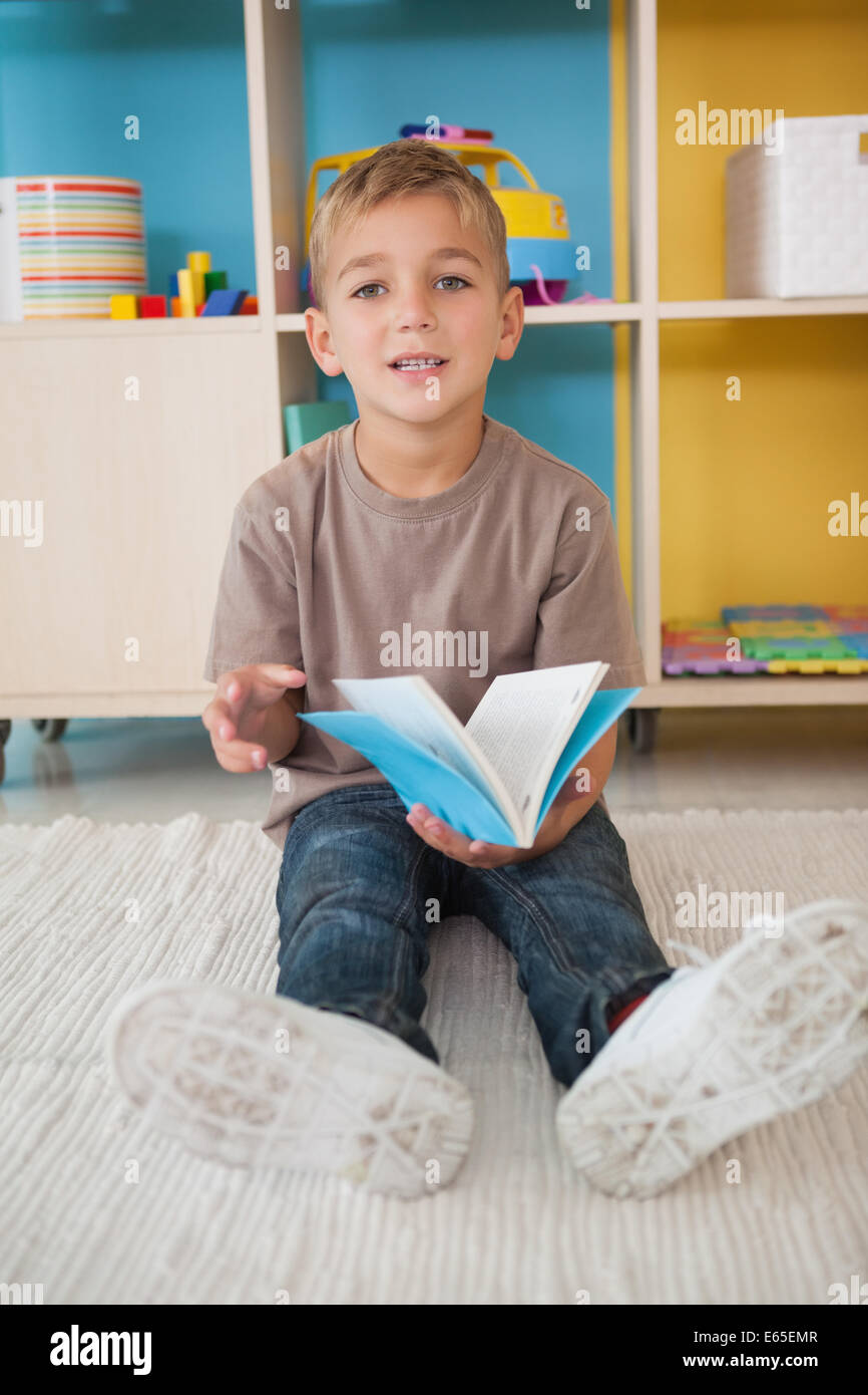 Cute little boy sitting on floor reading in classroom Stock Photo - Alamy