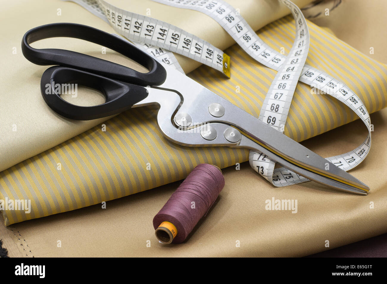 Tailoring scissors, spool of thread and white measuring tape on fabric ...