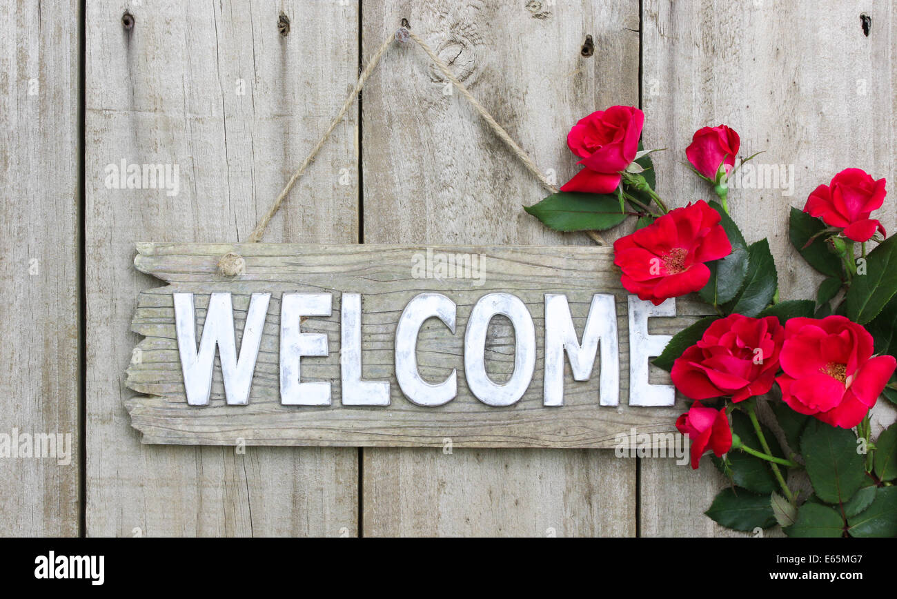 Distressed welcome sign hanging on wood fence with flower border of red ...