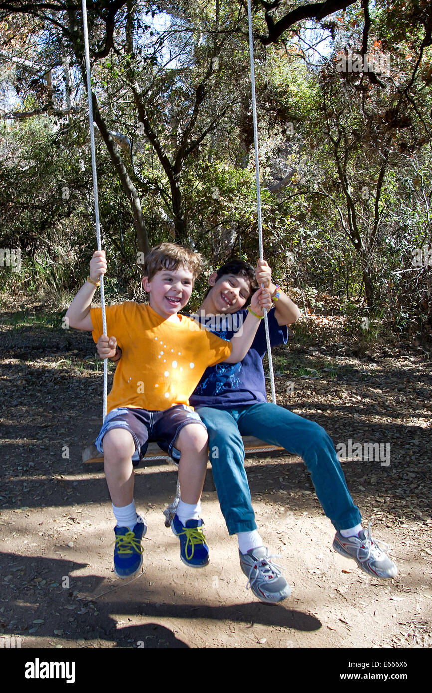 Two boys playing in a nature park. They are on a rope swing hung from a ...