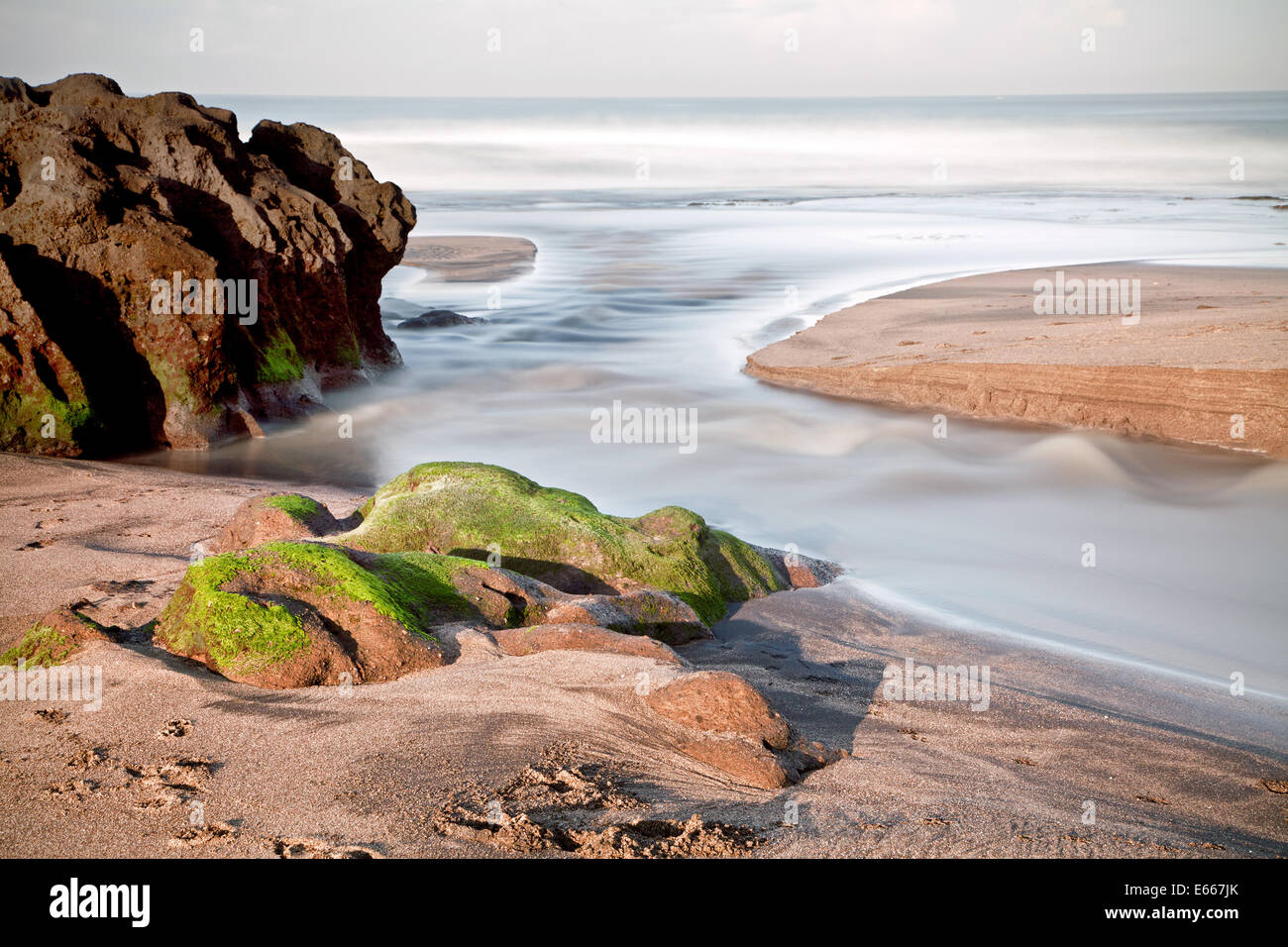 Bali beach scene with rivulet meandering and flowing into the sea ...