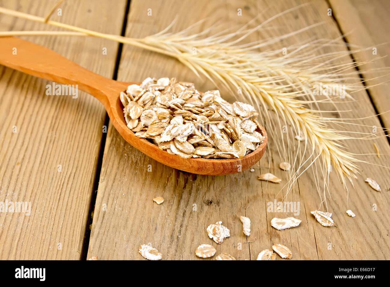 Rye flakes in wooden spoon, rye stalks on a wooden boards background ...
