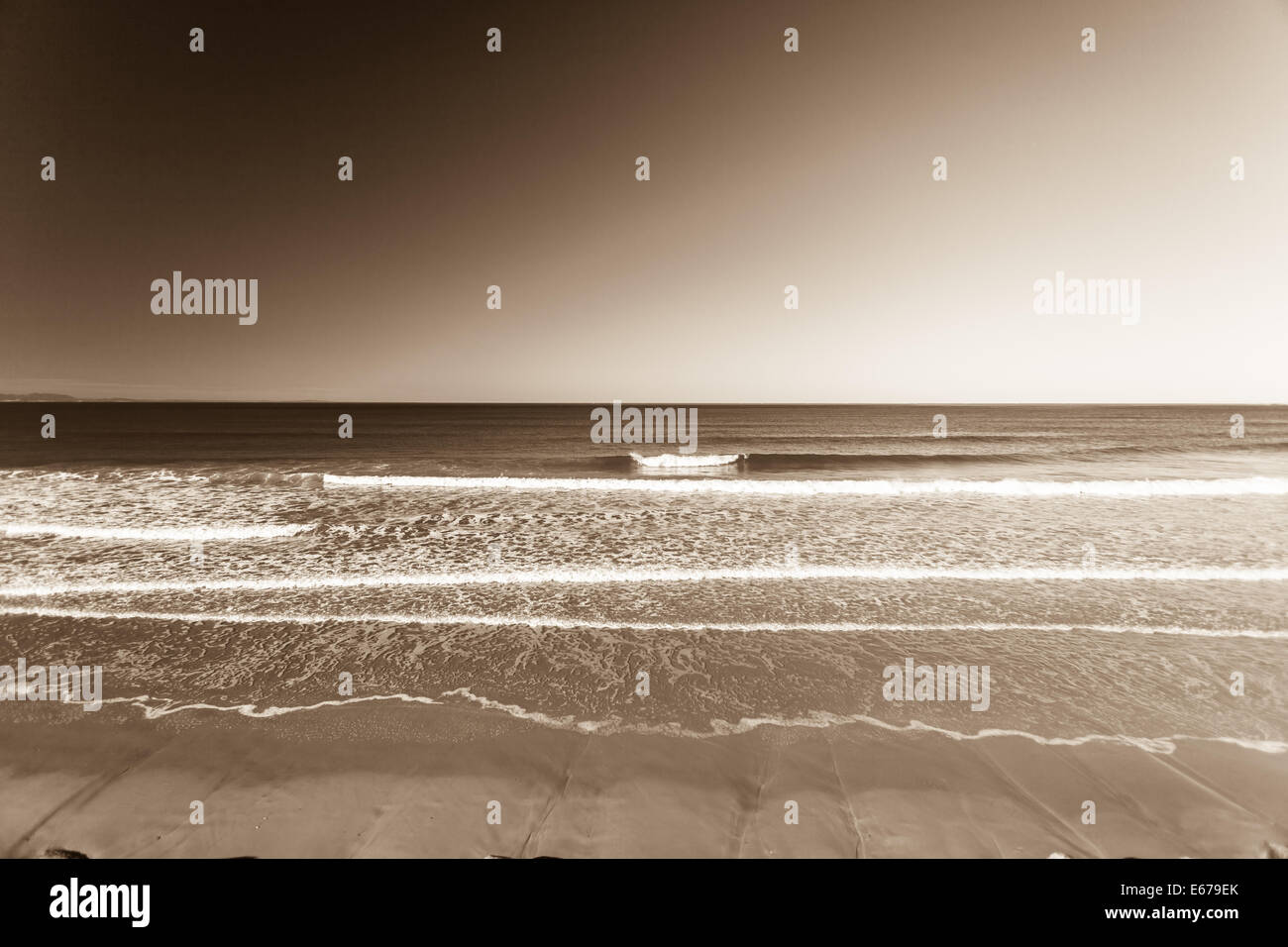 Beach sands into ocean water waves with distant ocean horizon in sepia ...