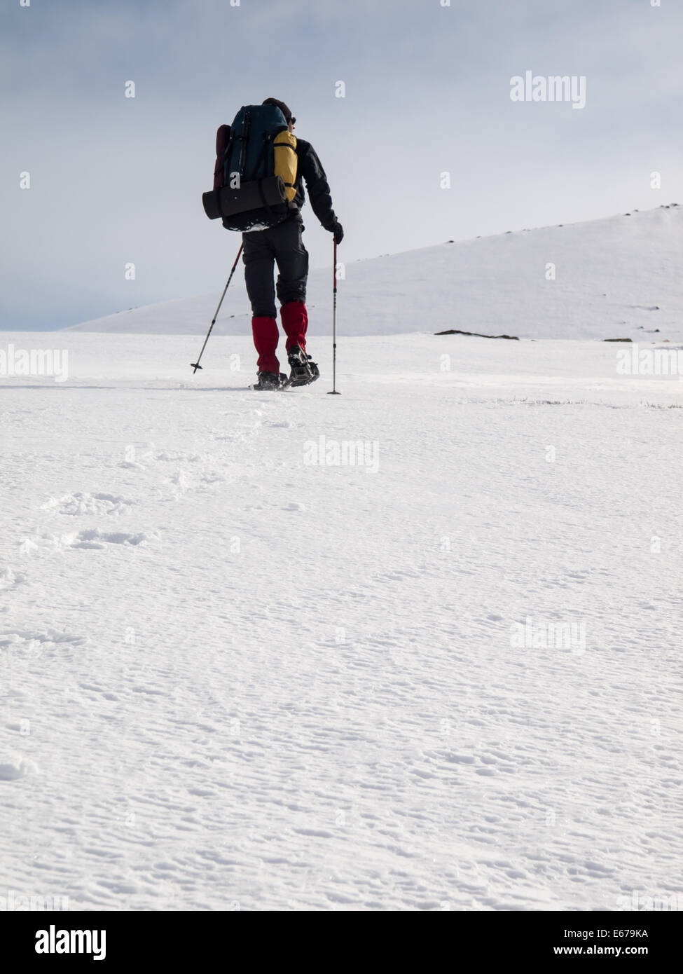 Man with heavy backpack snowshoeing in winter mountain landscape ...