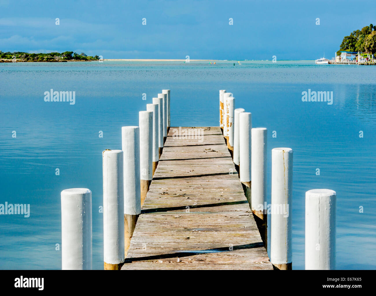 White posted small narrow jetty looking out across pale blue lake ...