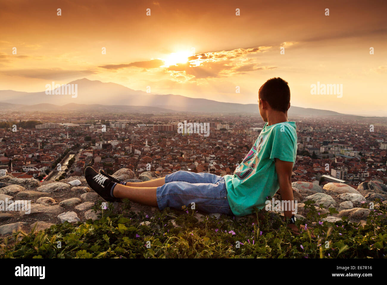 Laying relaxed boy looking to the city and to sunset Stock Photo - Alamy