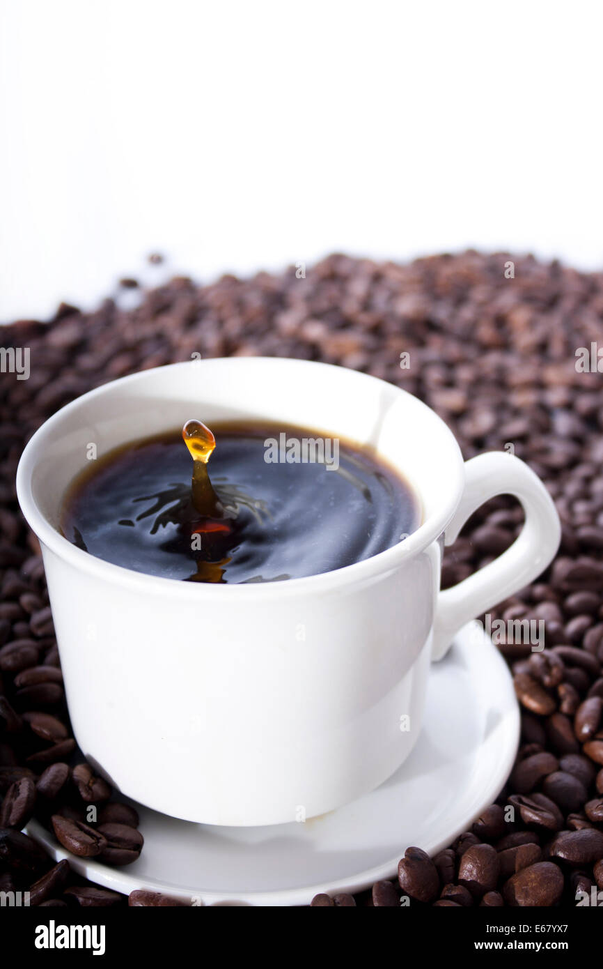 Drop of coffee in cup amongst coffee beans Stock Photo - Alamy