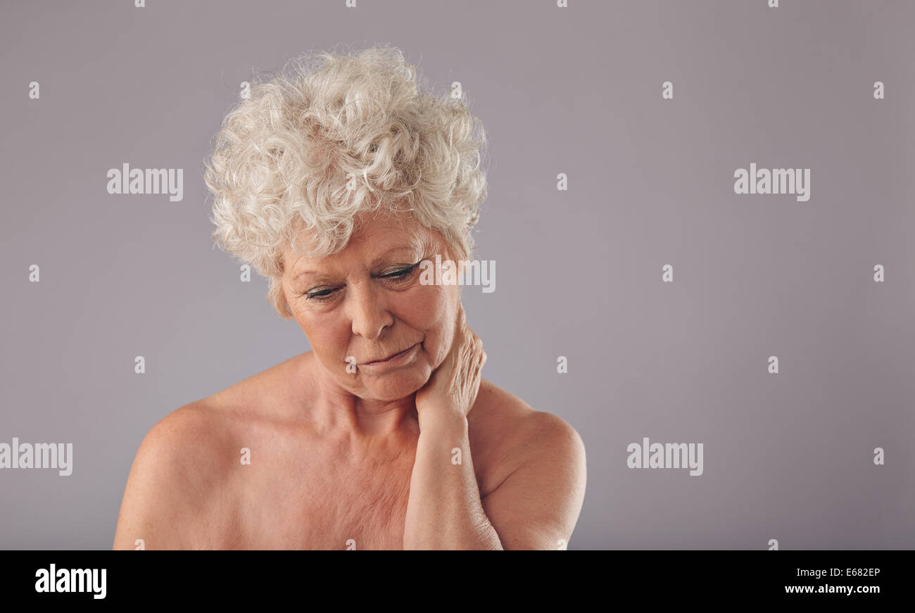 Studio shot of senior woman suffering from neck pain against grey ...