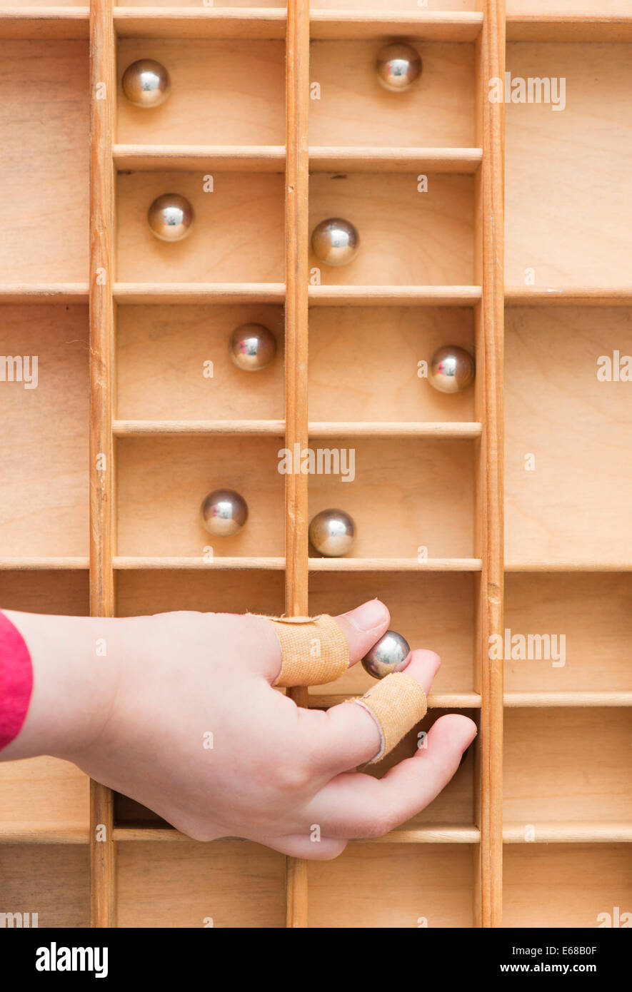 Hand of child placing small steel balls in wooden box with compartments ...