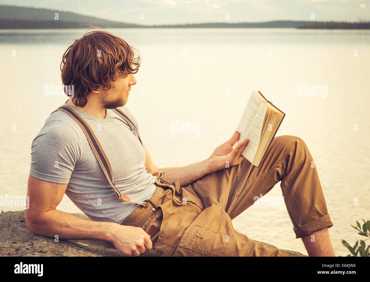 Young Man reading book outdoor with lake on background Summer vacations ...