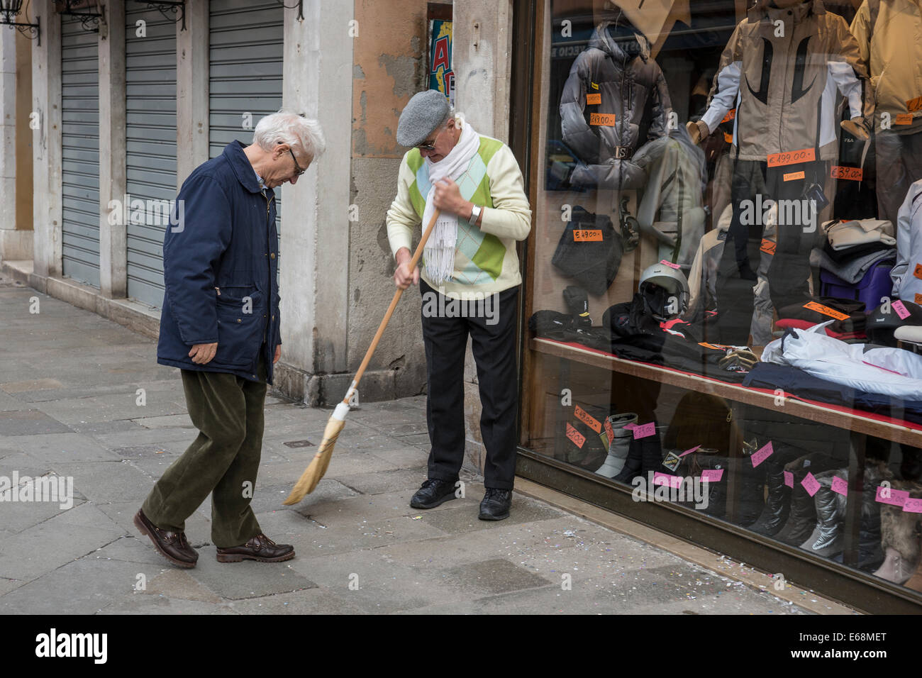 Two older men talk during morning sweeping in front of shop on a main ...