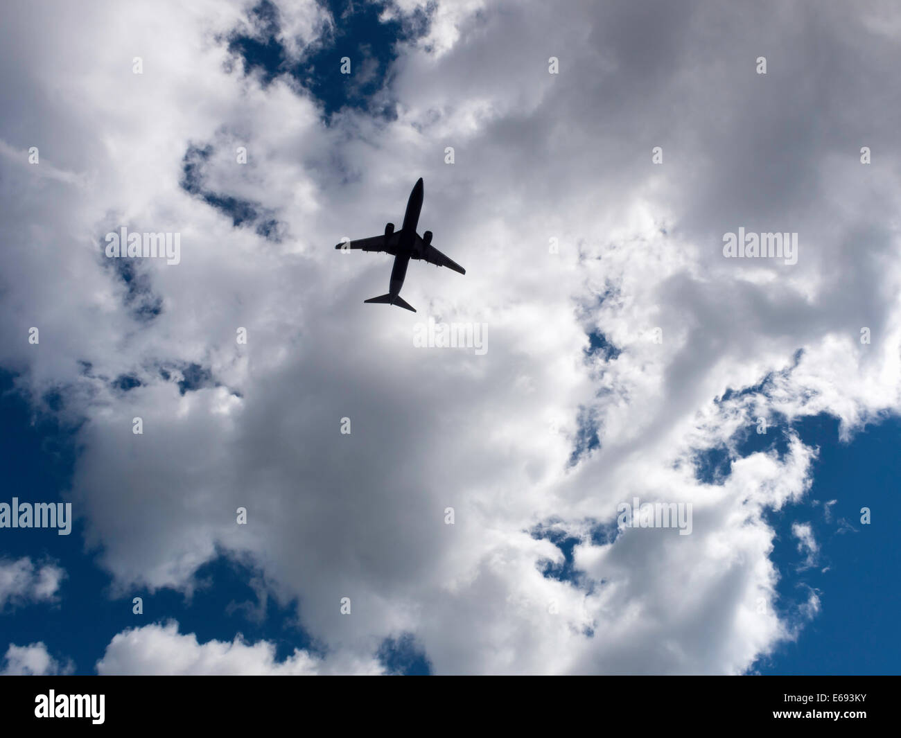 A twin engined commercial aircraft in silhouette flying below clouds ...