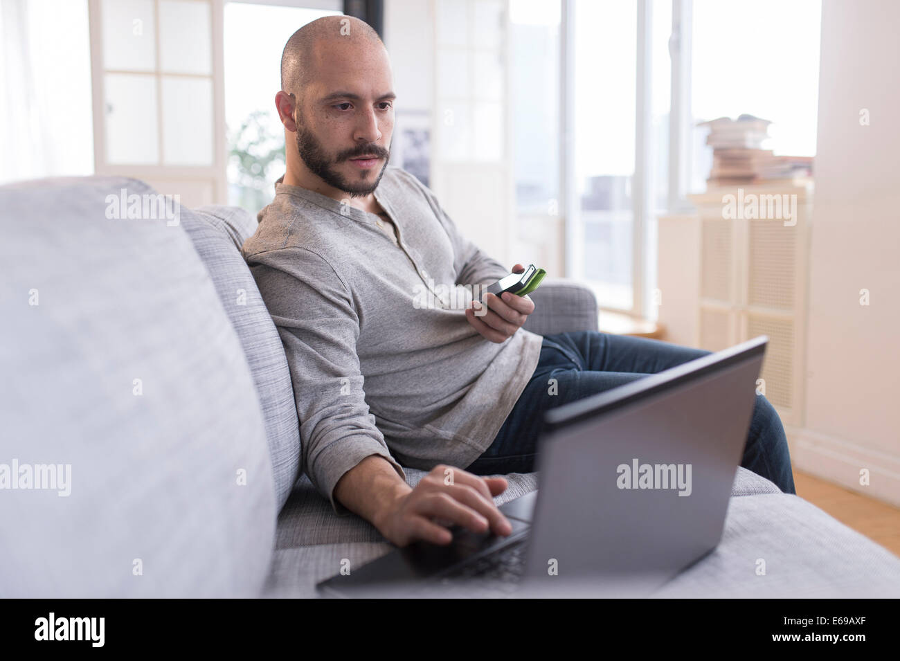 Hispanic man using cell phone and laptop on sofa Stock Photo - Alamy