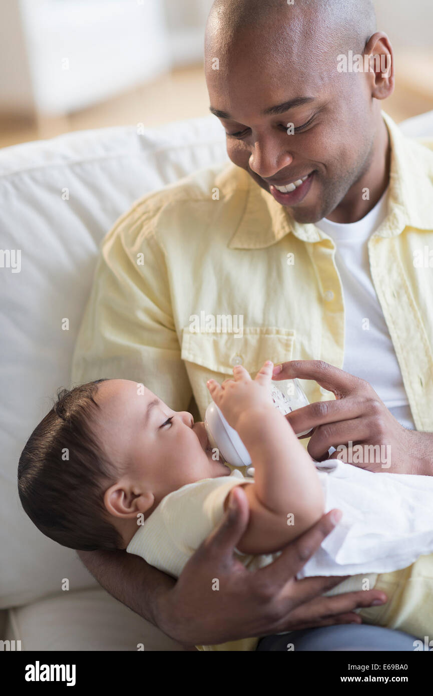 Smiling father feeding baby on sofa Stock Photo - Alamy