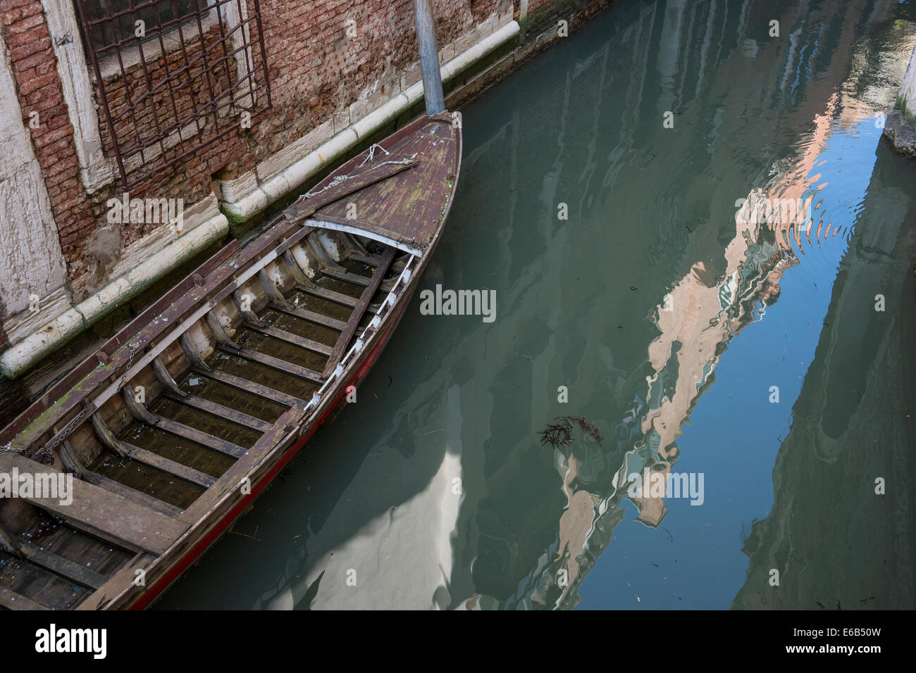 An old work boats moored along a side canal in Venice with reflections ...